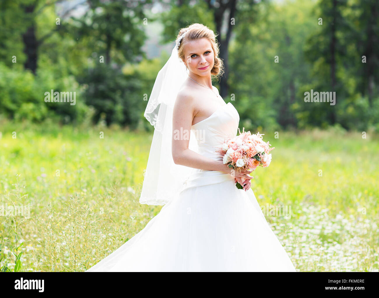 Beautiful bride with wedding bouquet of flowers outdoors in green park ...