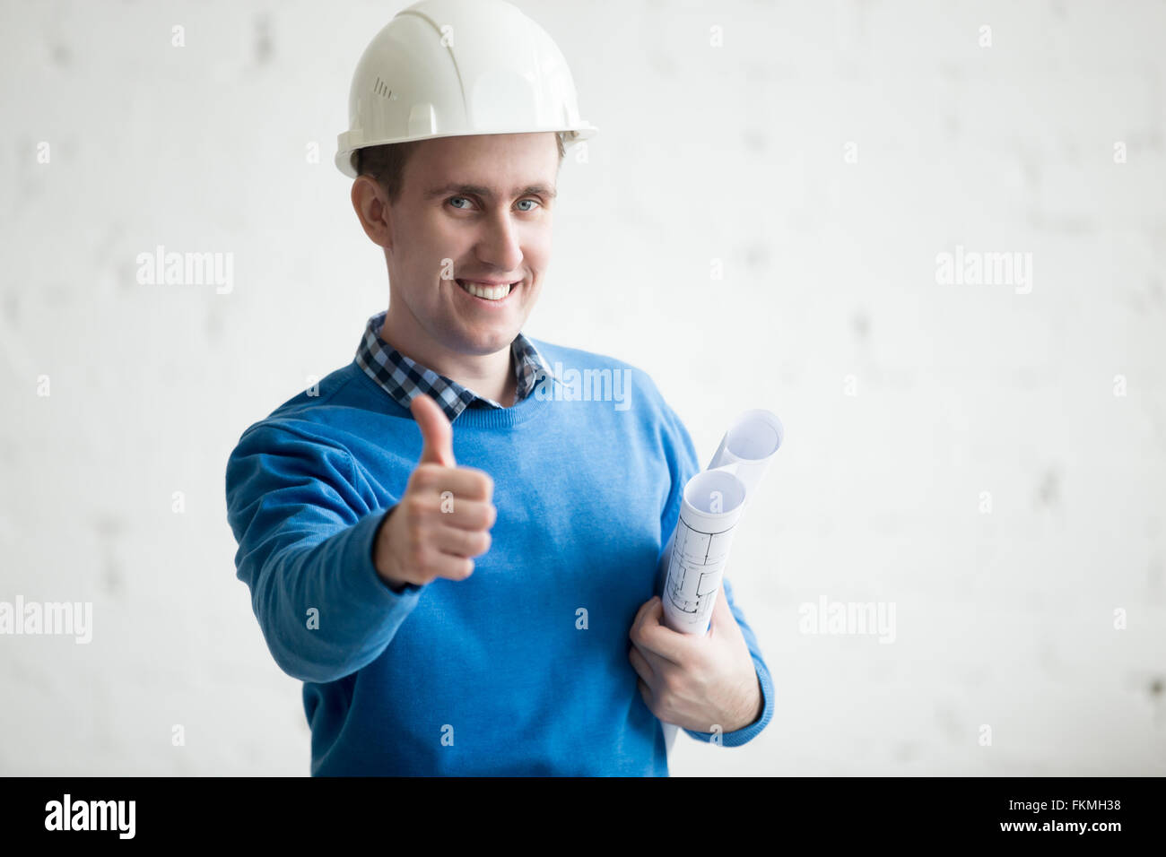 Portrait of young cheerful handsome engineer in white hard hat holding ...