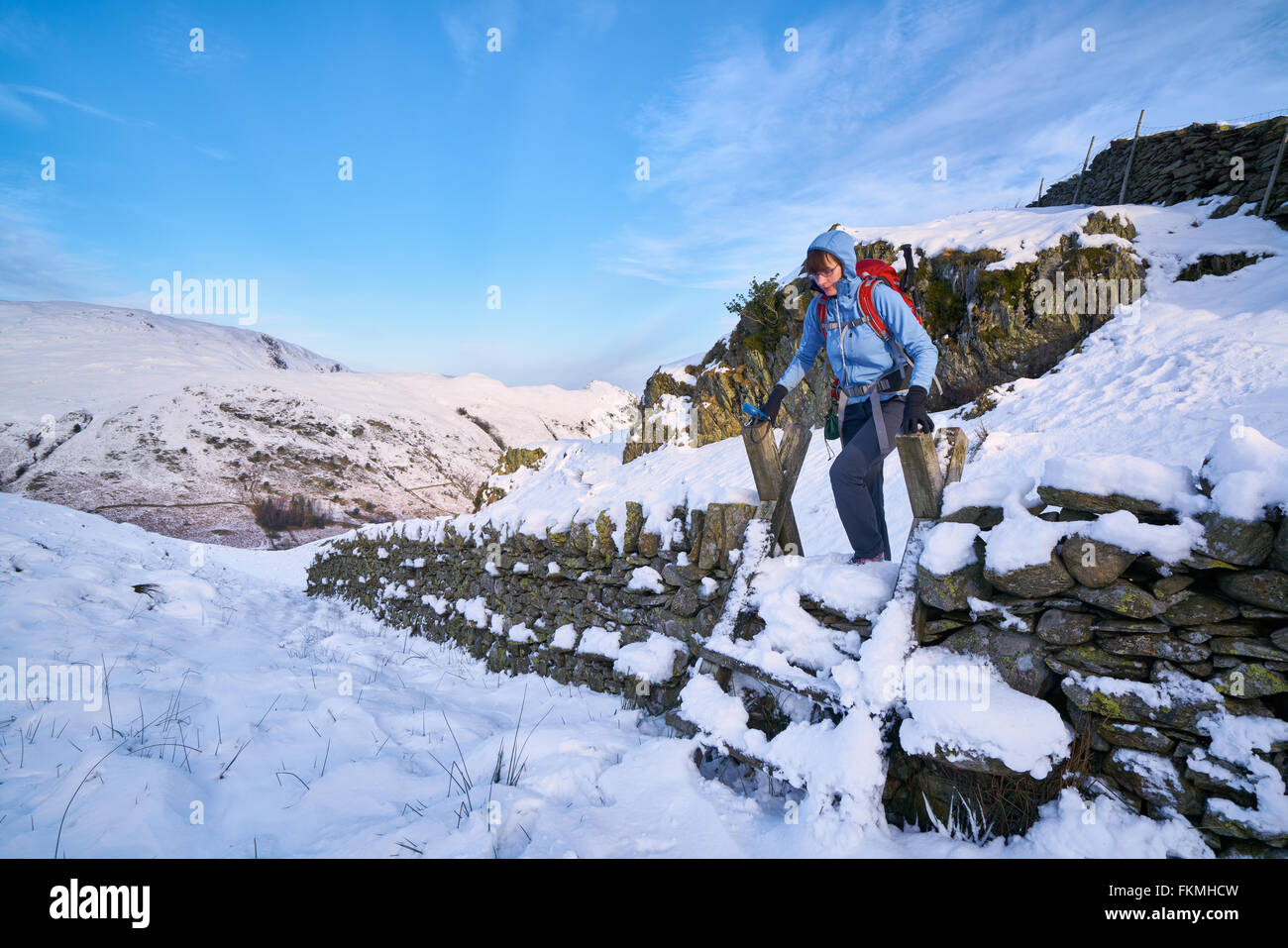Hiker crossing a stile over a stone wall at Hartsop Above How in the ...