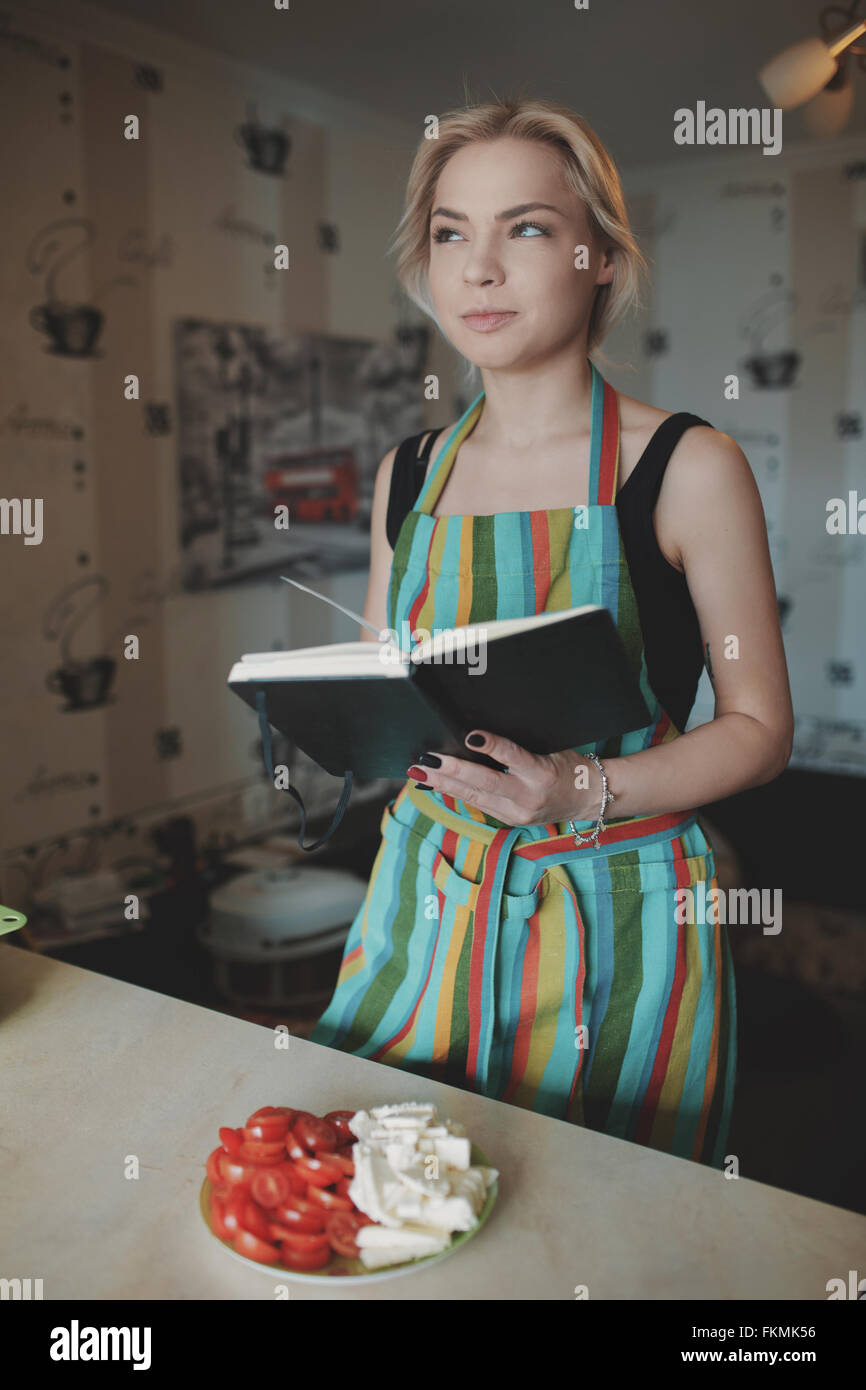 Young woman looking up in a recipes book Stock Photo - Alamy