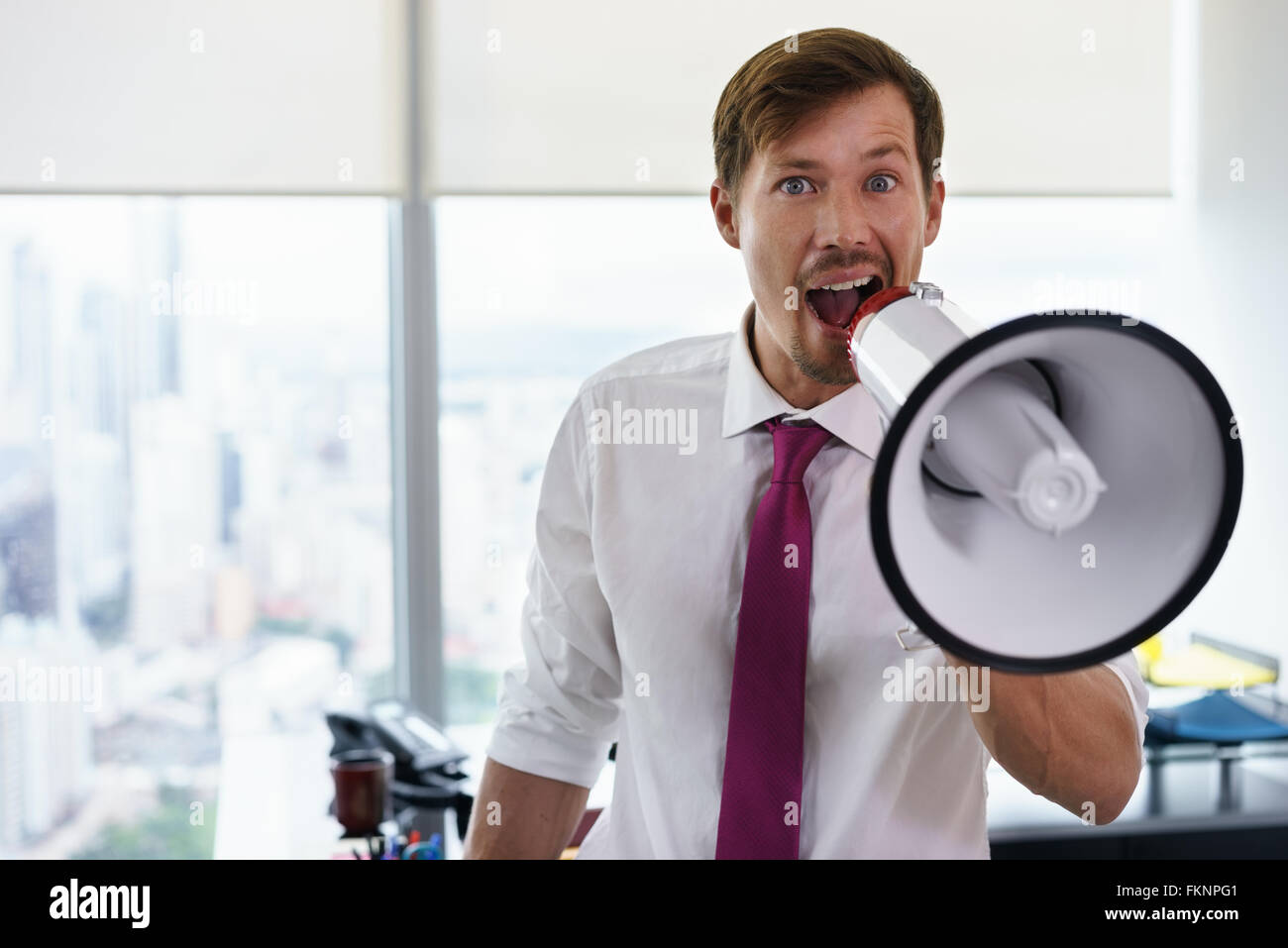 Young executive office worker holding megaphone and speaking at camera ...
