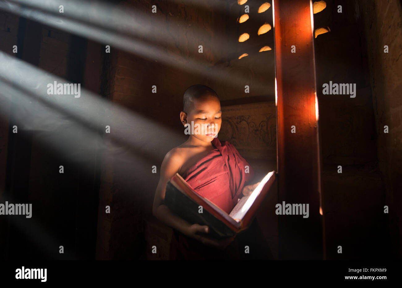 A young monk reading with rays of sunlight in the temples of Bagan ...
