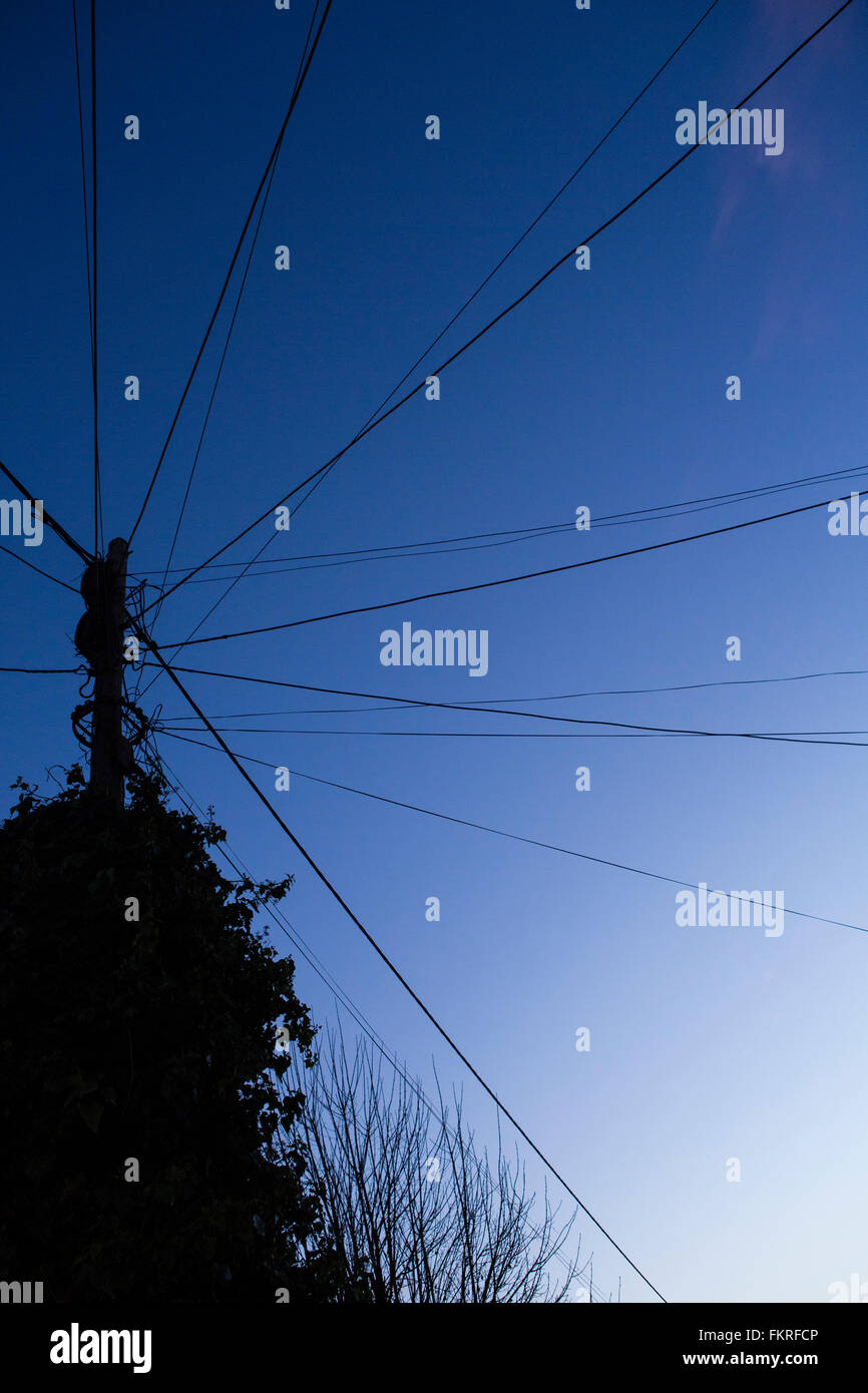 Telephone and power cables hanging from a pole set againsta deep blue ...