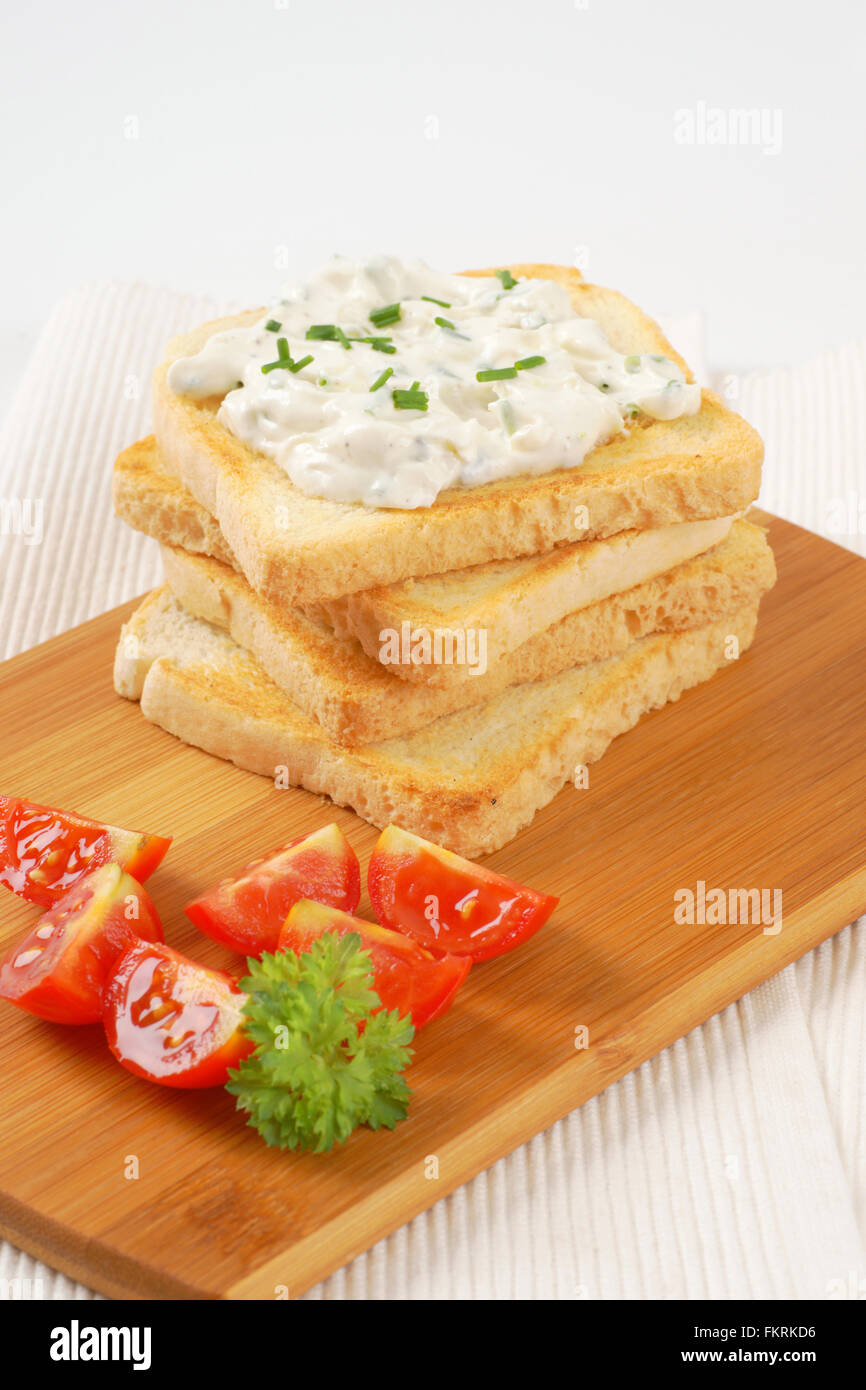 stack of fresh toasts with chives spread on wooden cutting board and ...