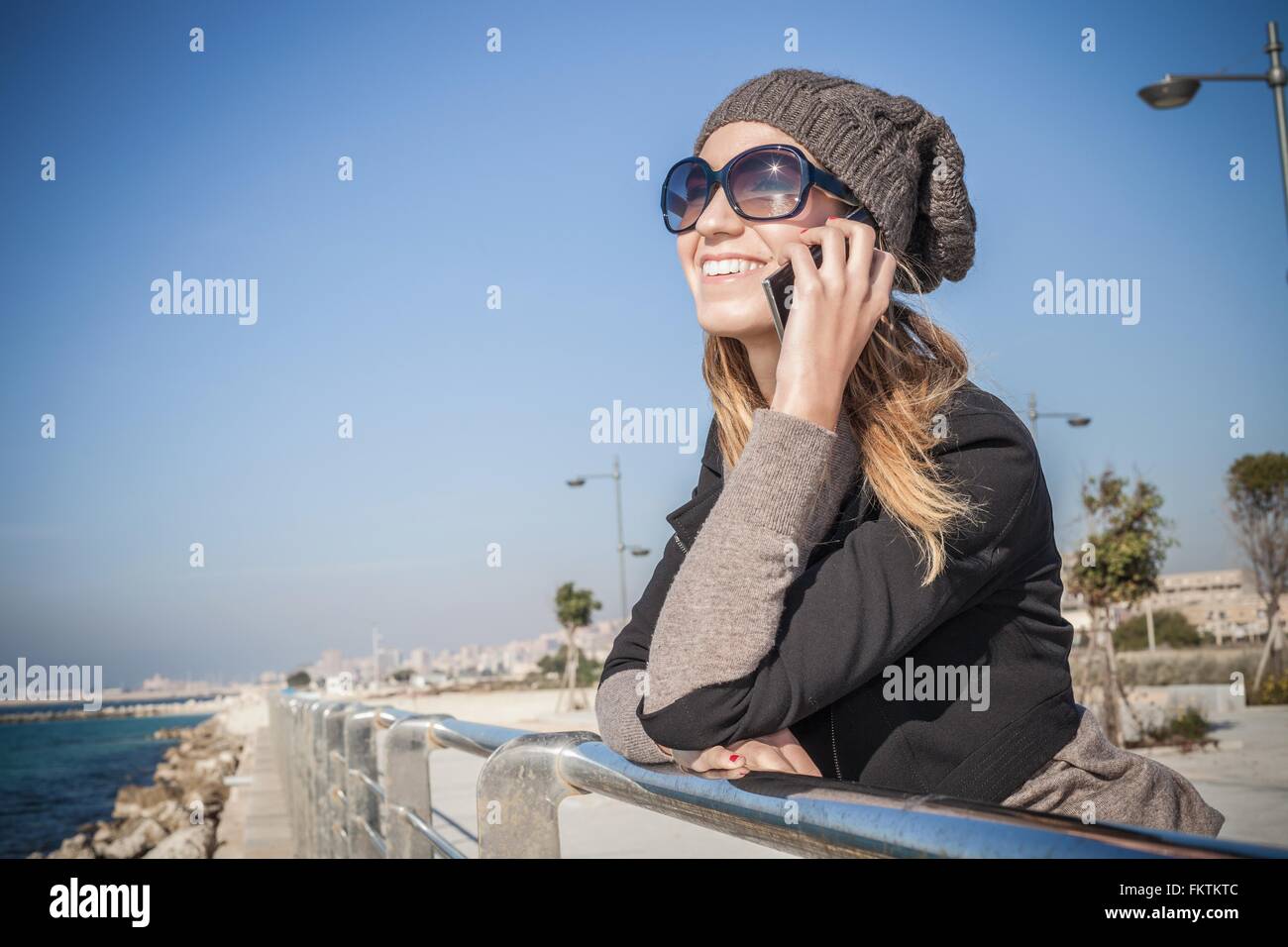 Side view young woman leaning against railings using smartphone smiling ...