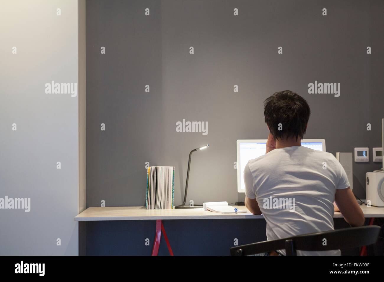 Rear view of man sitting at desk using desktop computer Stock Photo - Alamy