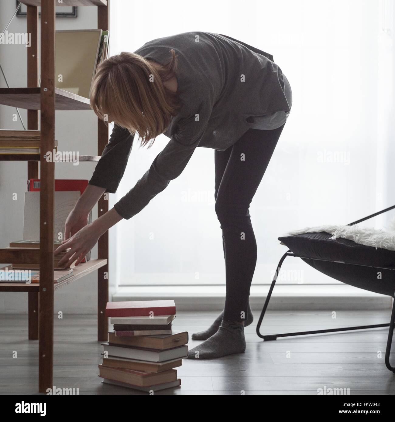 Woman bending forward to arrange books on living room bookshelf Stock ...