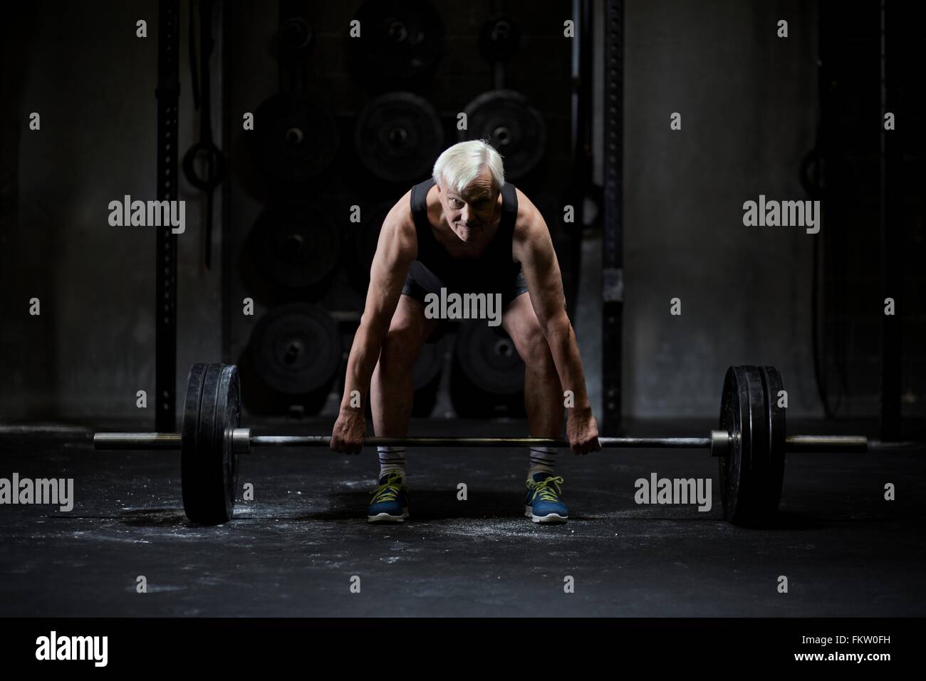 Senior man preparing to weightlift barbell in dark gym Stock Photo - Alamy