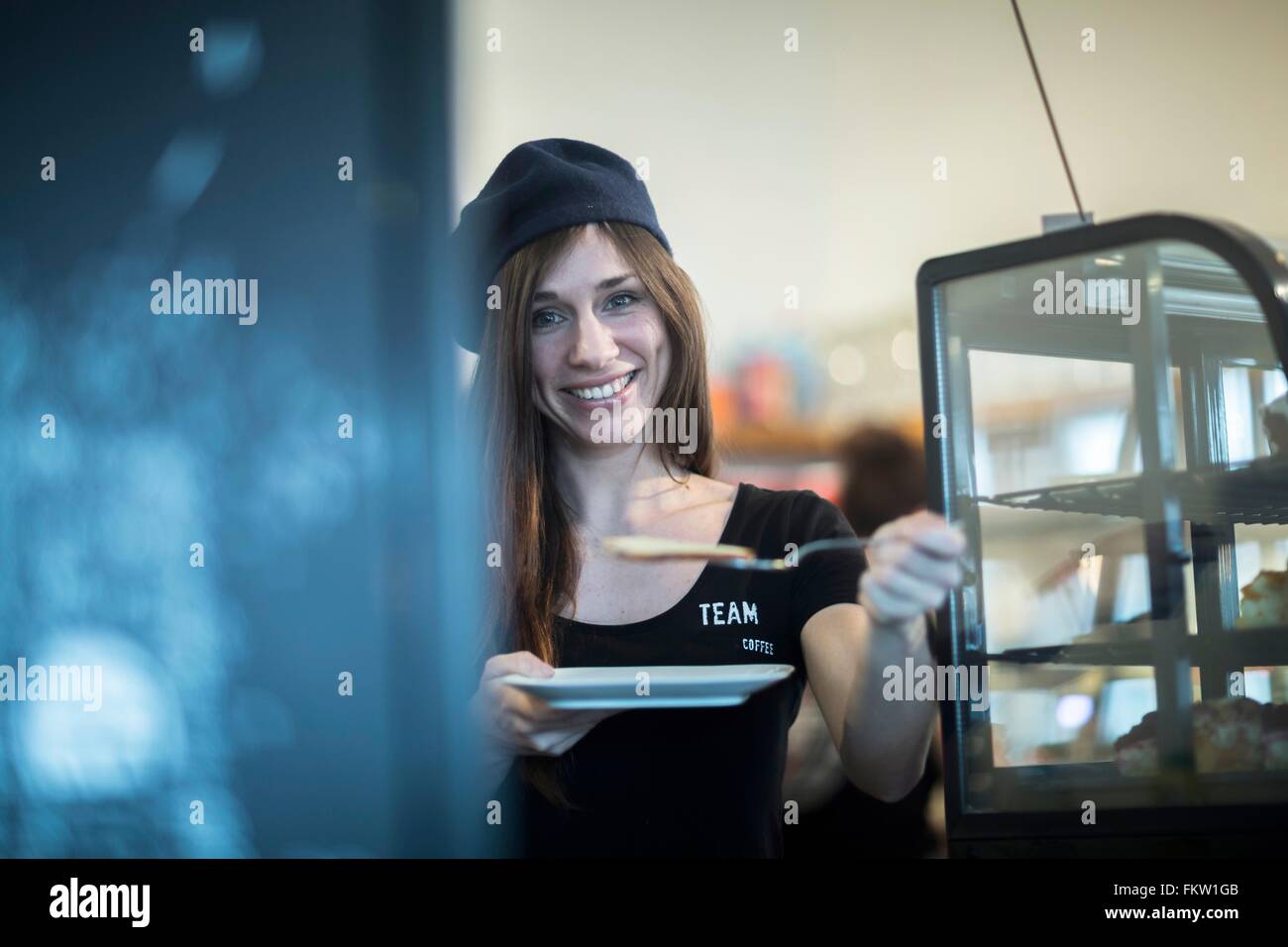 Portrait of young female waitress holding plate and cake slice in cafe ...