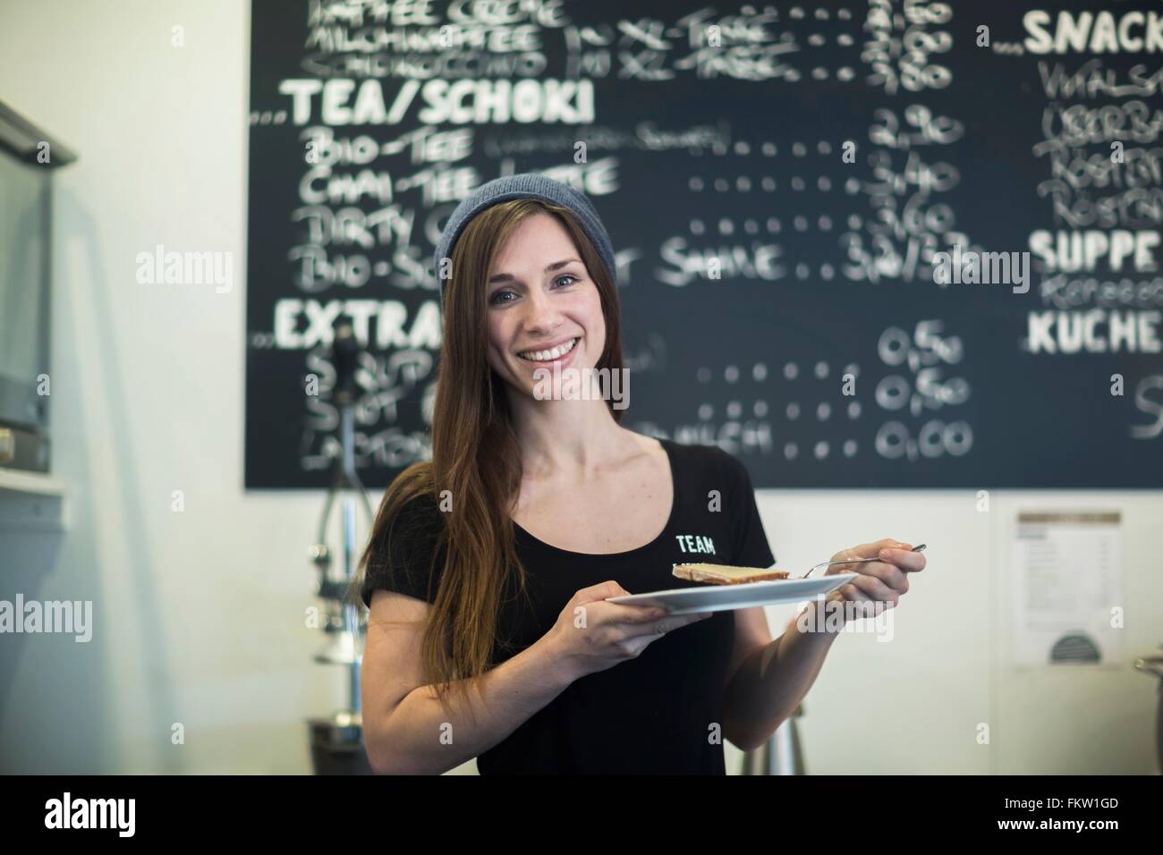 Portrait of young female waitress holding plate and cake slice in cafe ...
