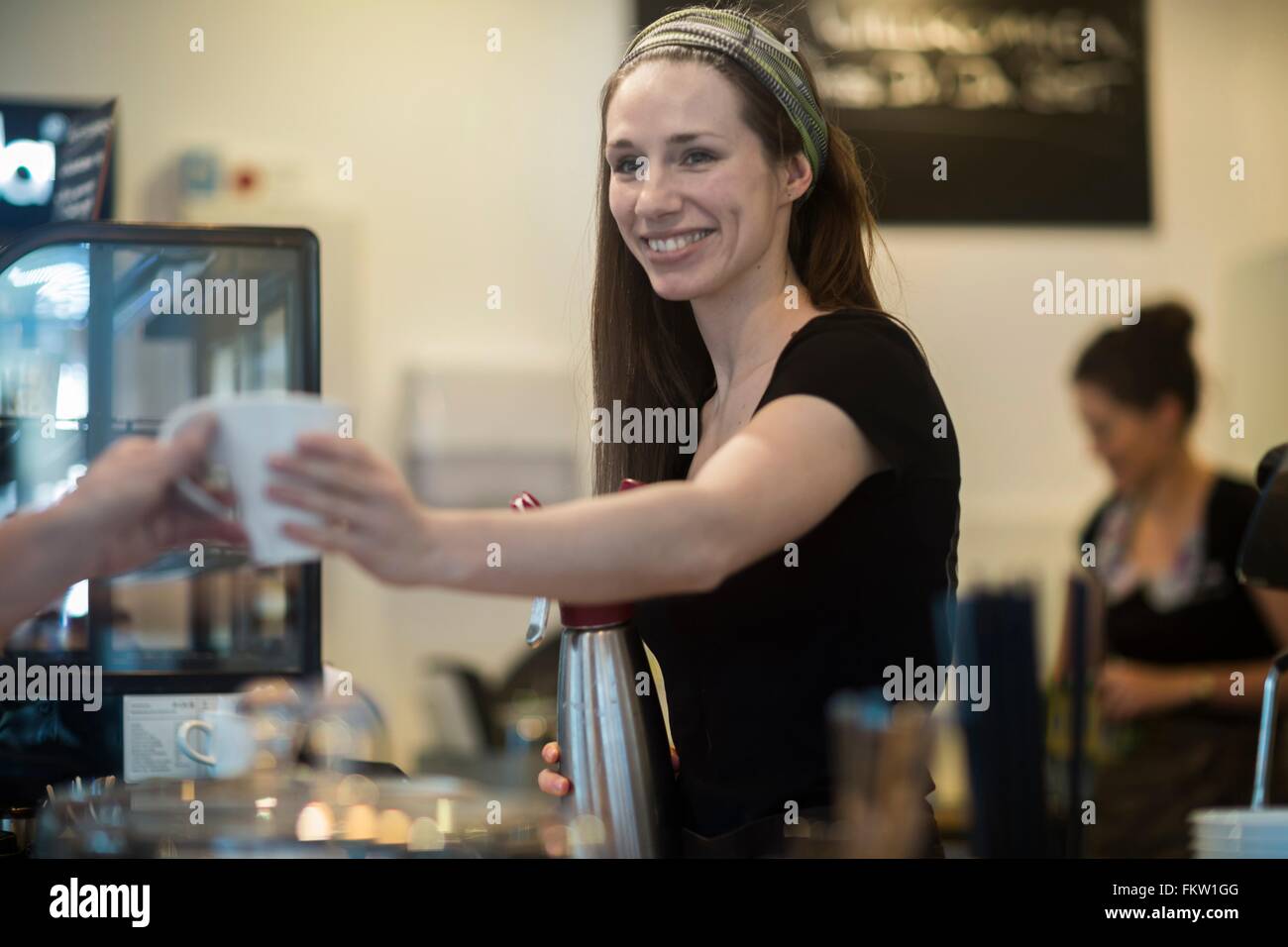 Young female waitress handing cup of coffee to cafe customer Stock ...