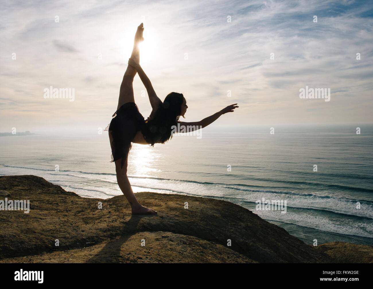 Young female dancer standing on rock, holding leg, stretching in ...