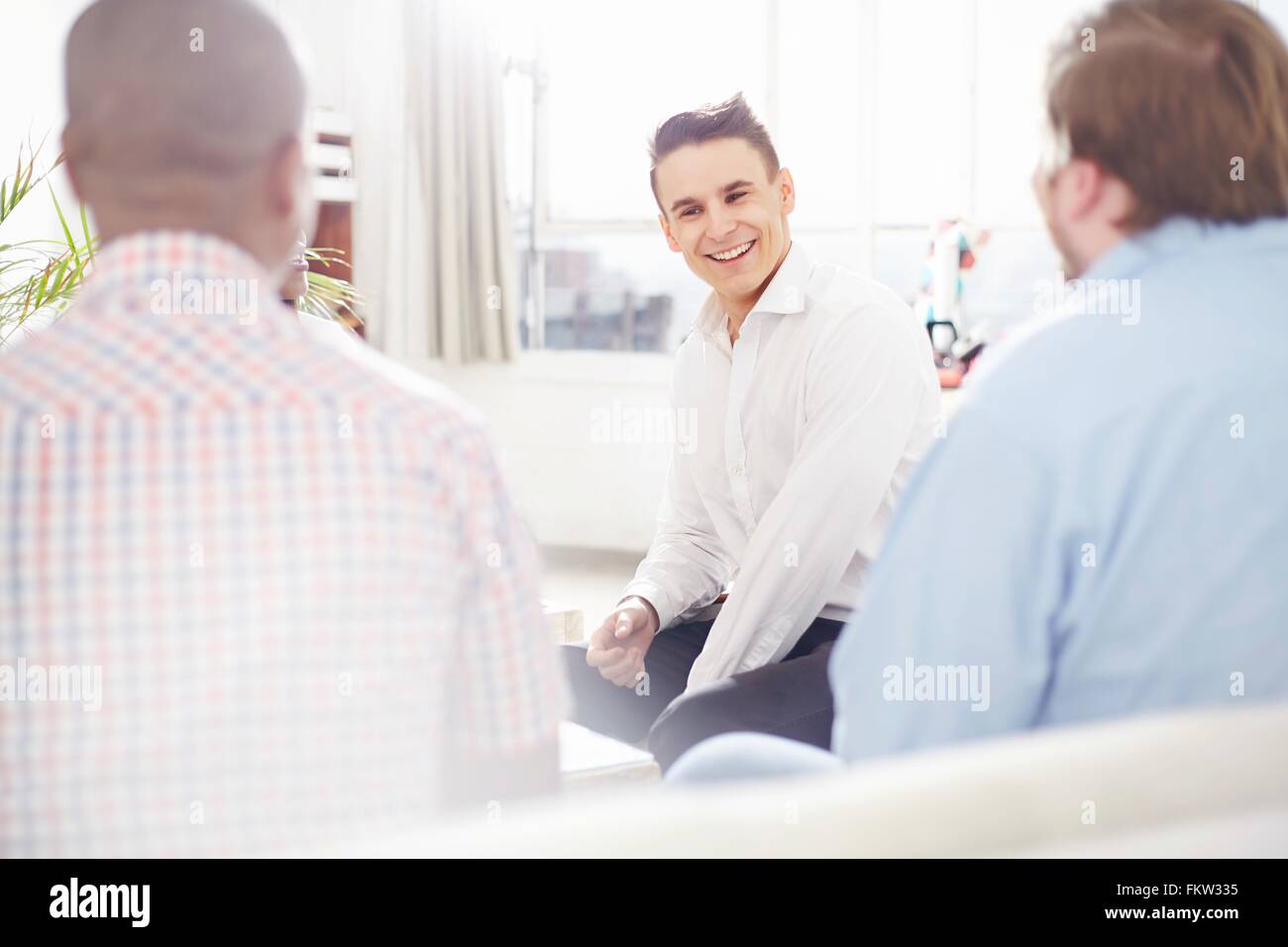 Young man in fice talking to colleagues smiling Stock Photo - Alamy