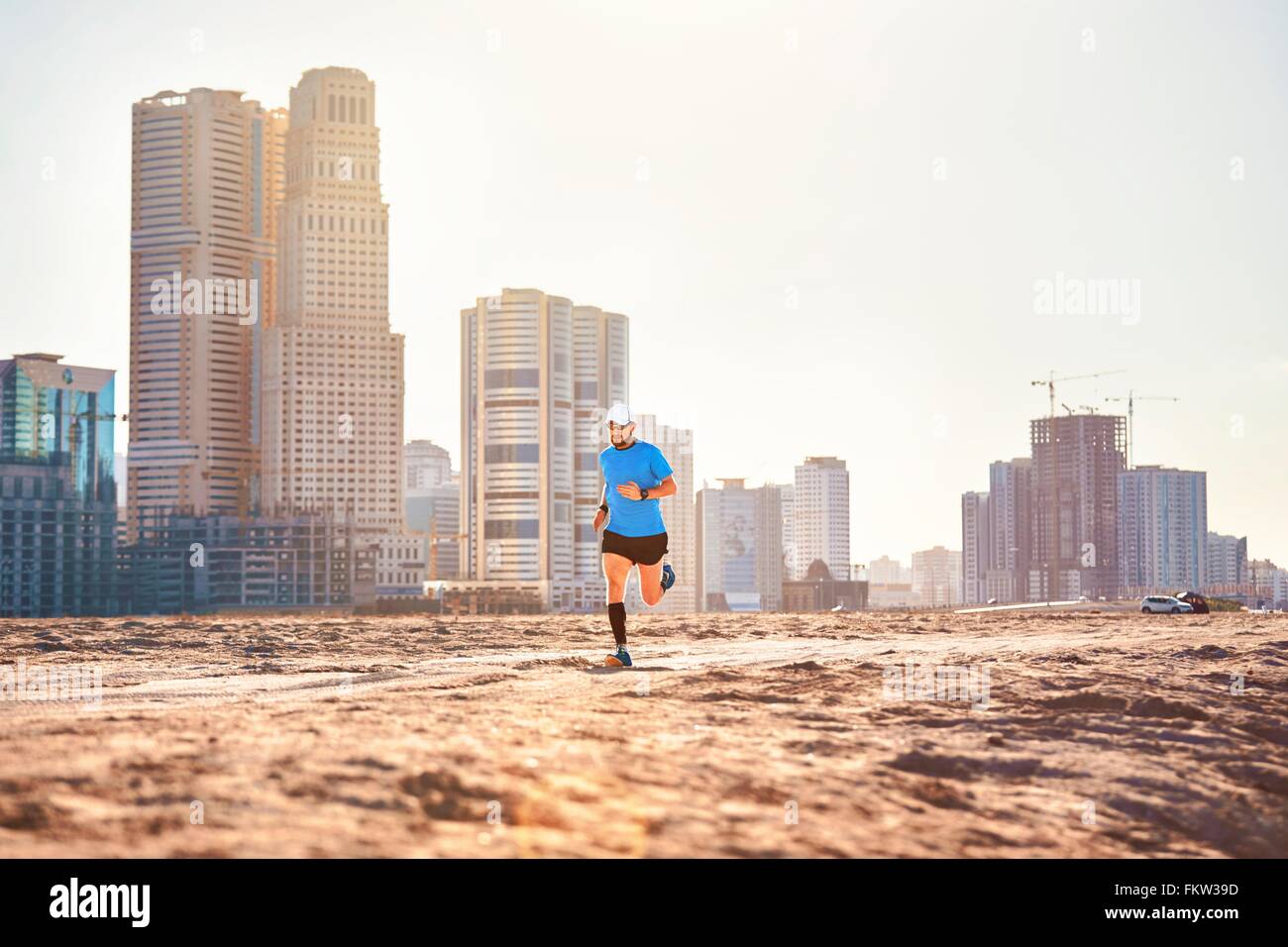 Mid adult man running on sand by skyscrapers, Dubai, United Arab ...