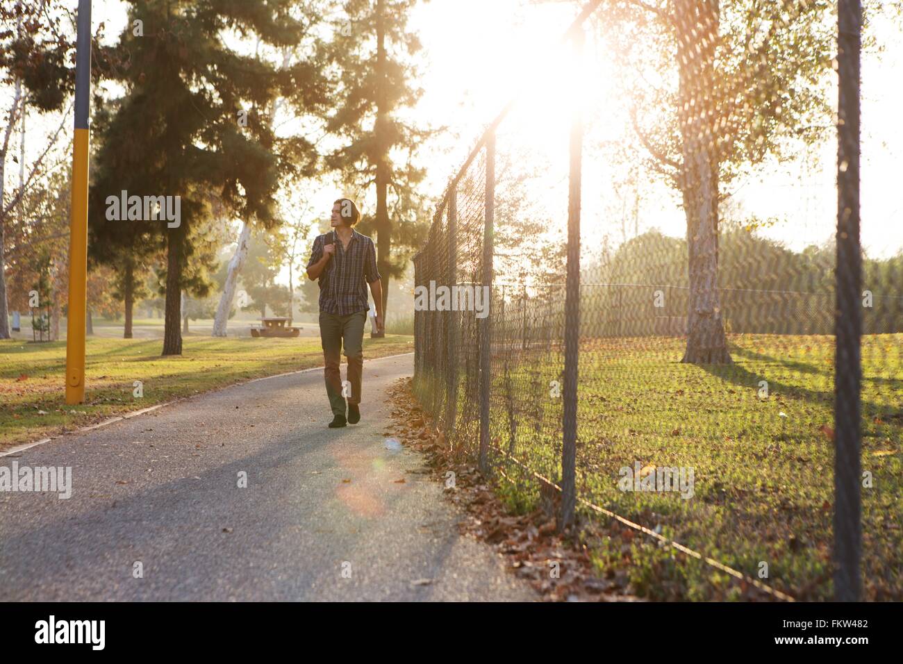 Full length front view of young man walking on pathway through park ...