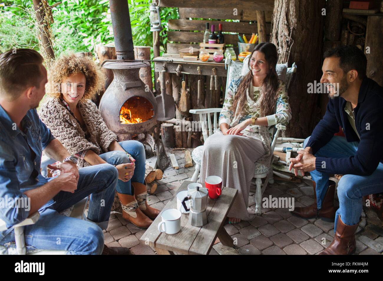 Four adult friends drinking coffee in open cabin with wood stove Stock ...