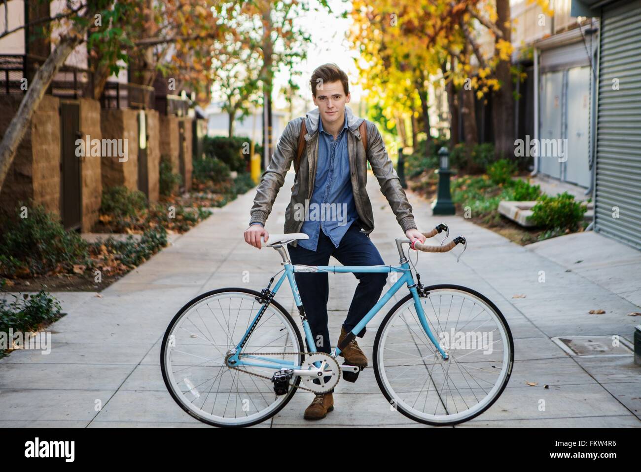 Portrait of young man leaning against cycle on sidewalk Stock Photo - Alamy