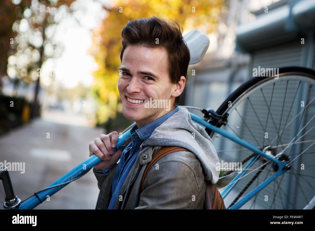 Portrait of young man carrying cycle on shoulders along sidewalk Stock ...