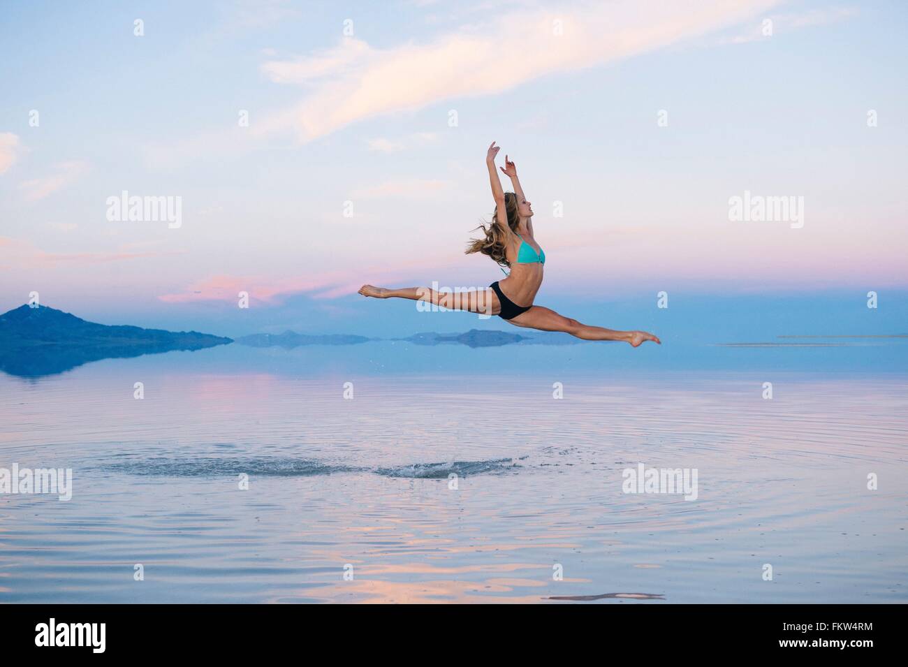 Female ballet dancer jumping mid air over lake, Bonneville Salt Flats ...