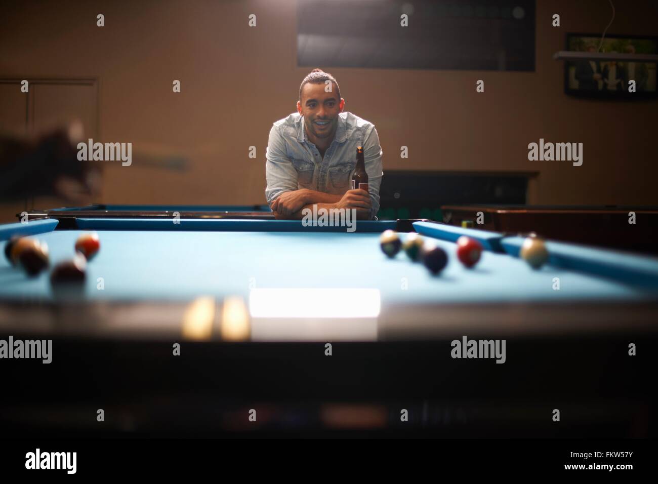 Man with beer leaning against pool table, smiling Stock Photo - Alamy