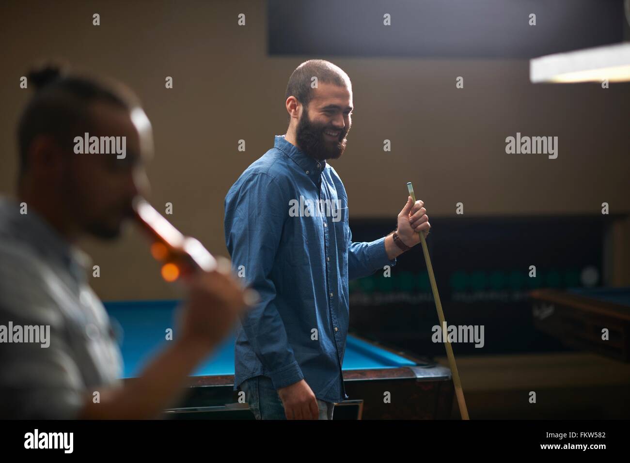 Man playing pool, friend drinking beer in foreground Stock Photo - Alamy