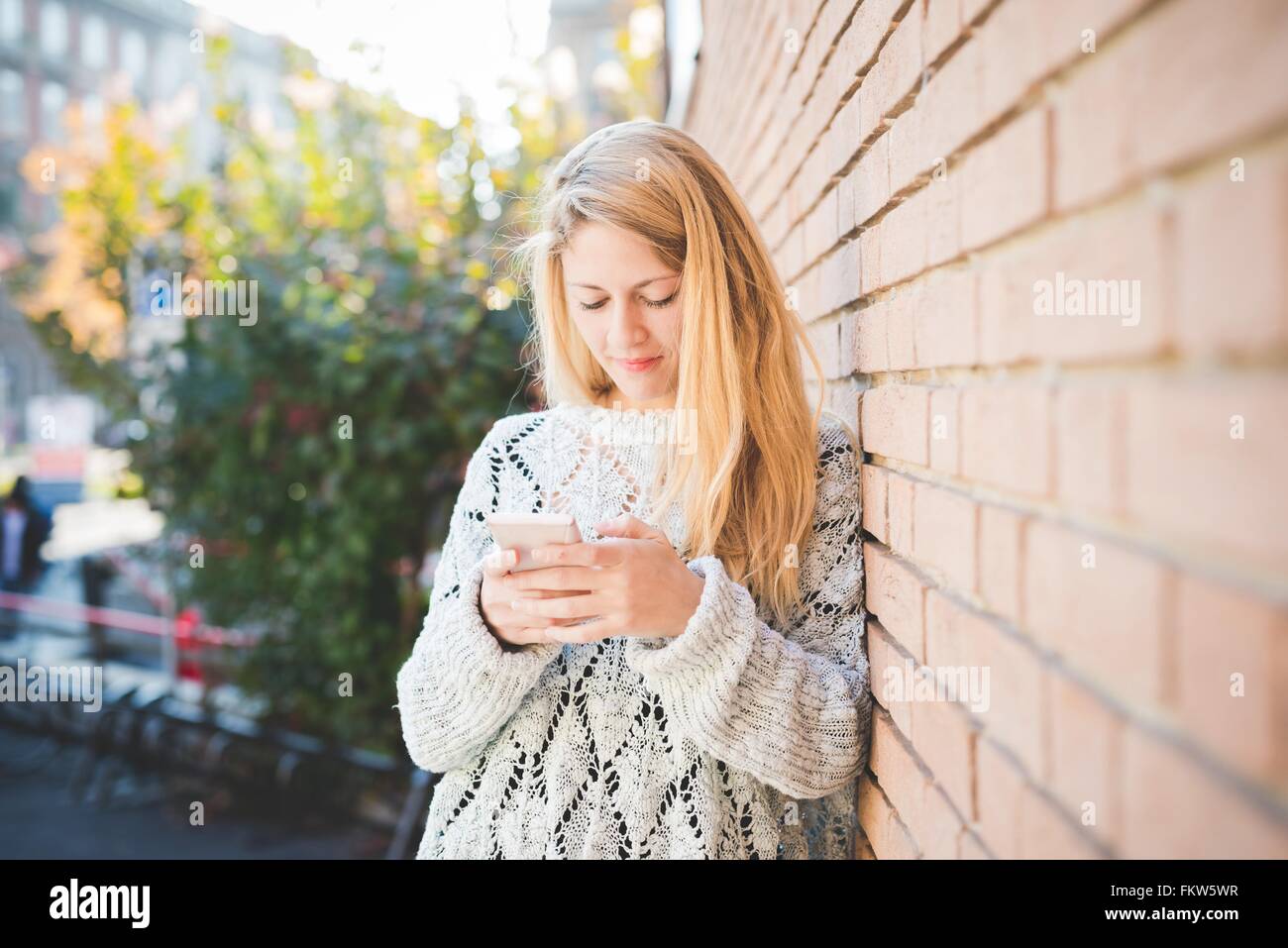 Woman texting on smartphone, against brick wall Stock Photo - Alamy