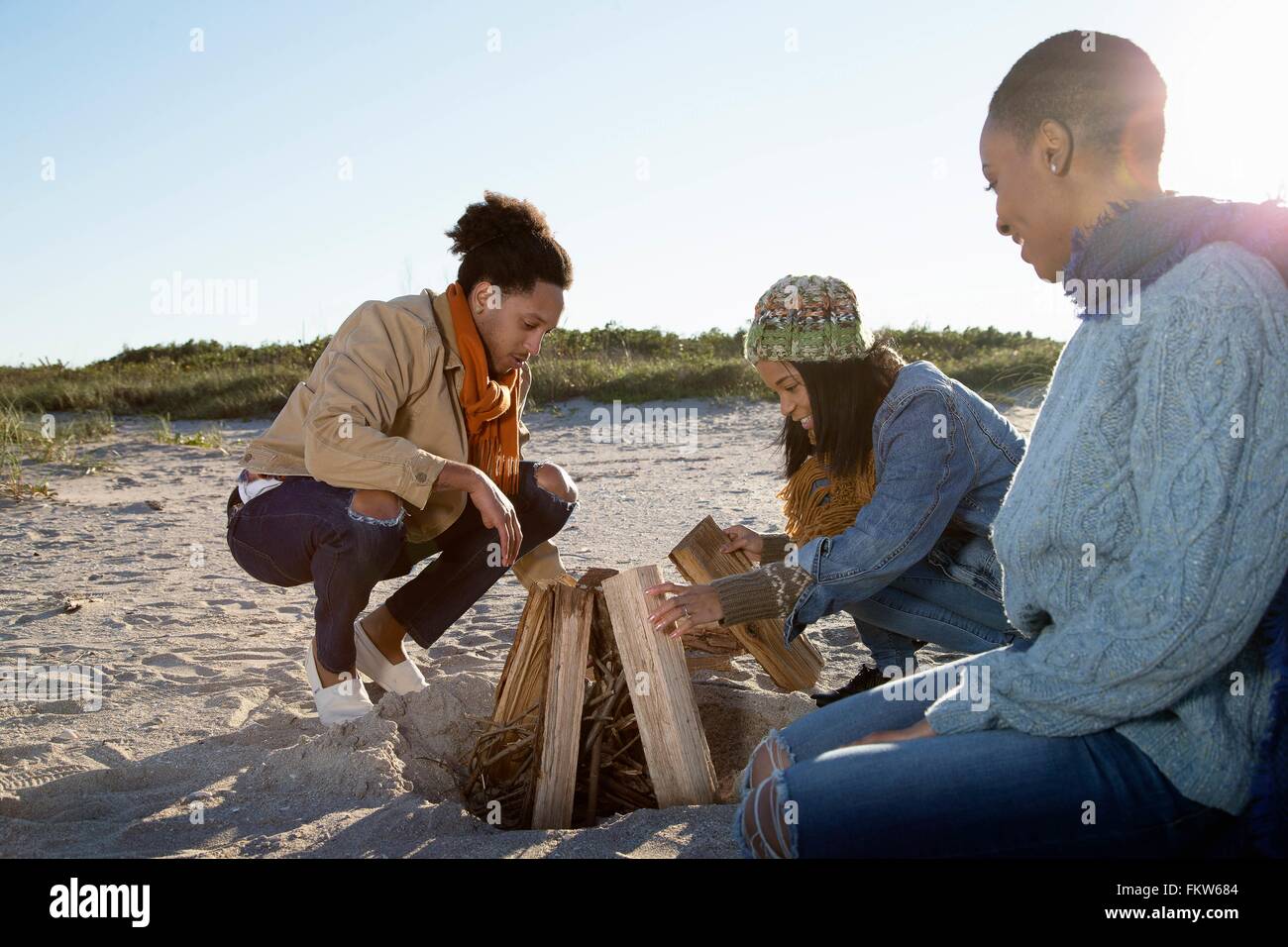 Three friends on beach, preparing camp fire Stock Photo - Alamy