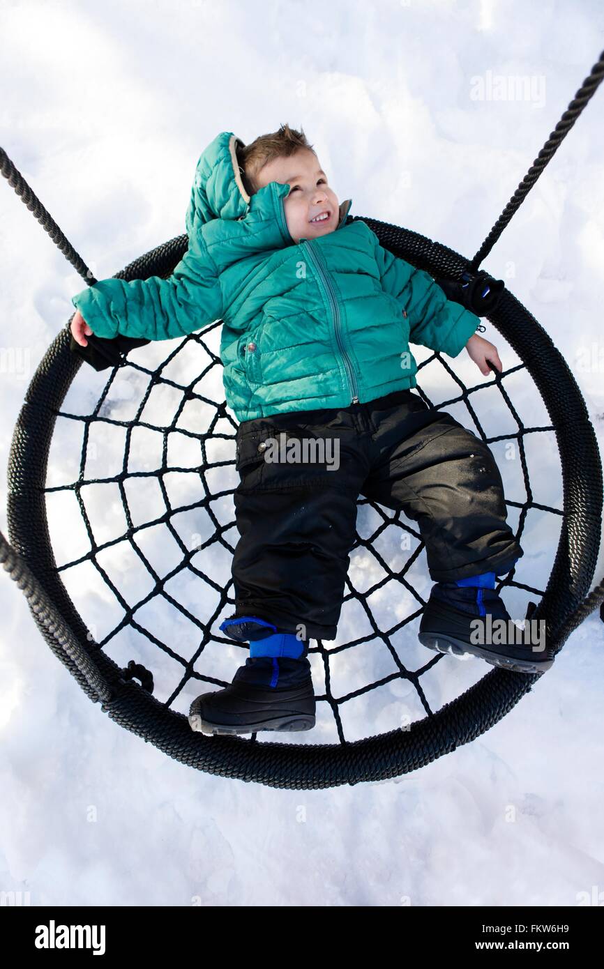 Overhead view of preschool boy lying on hammock swing in snow looking ...