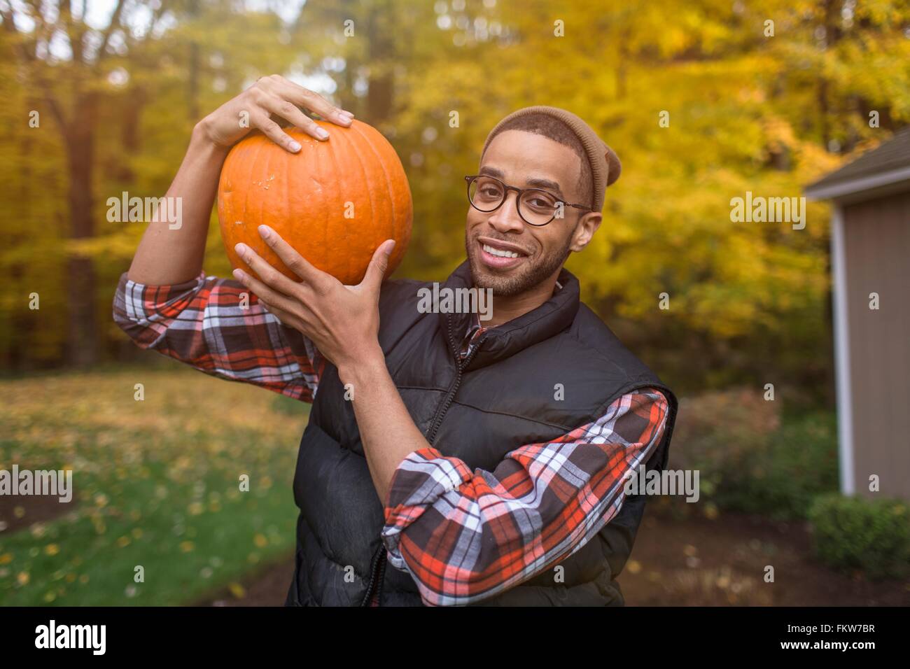 Portrait of mid adult man carrying pumpkin on shoulder in autumn garden ...