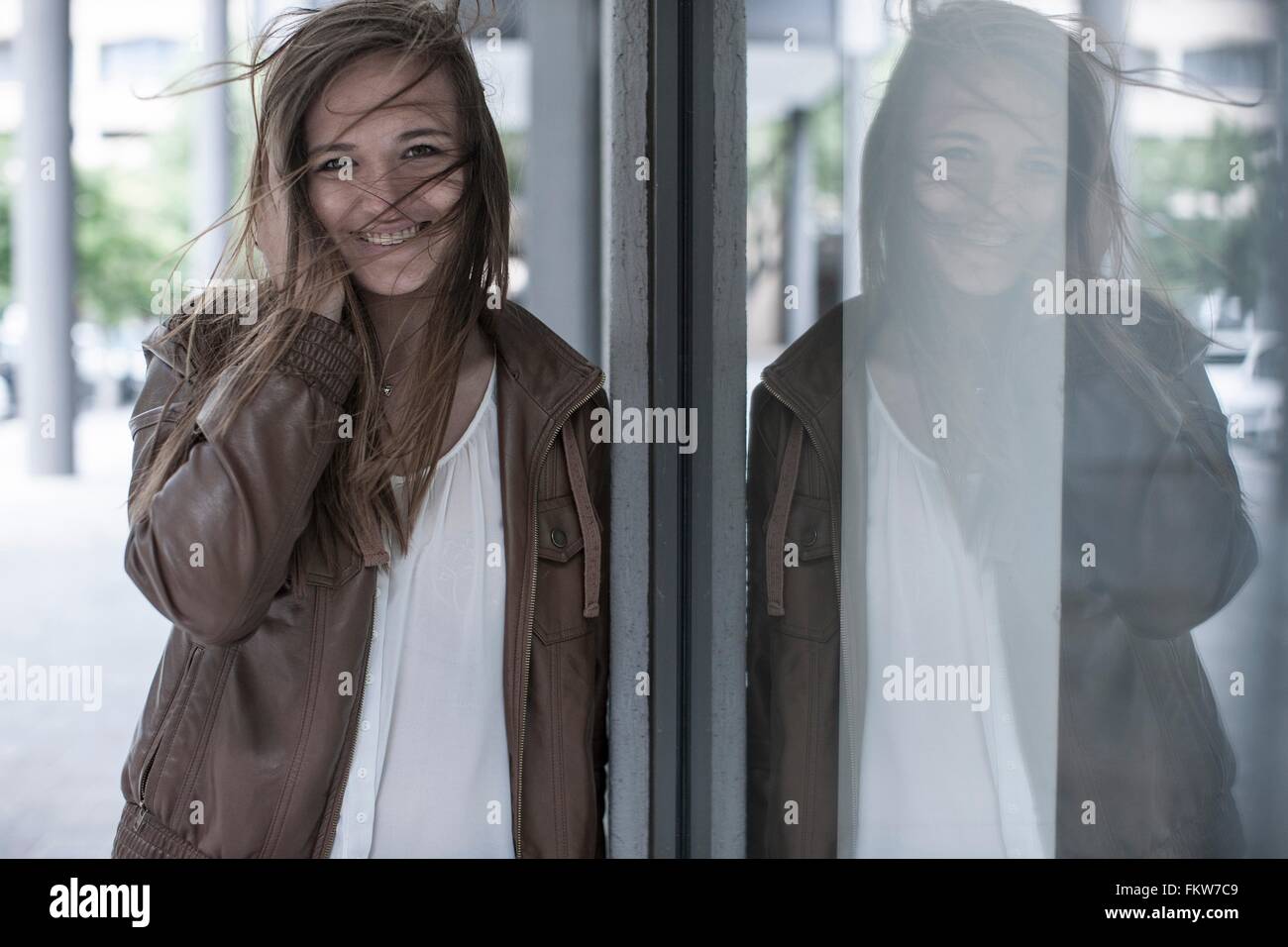 Portrait of teenage girl with flyaway hair leaning against city window ...
