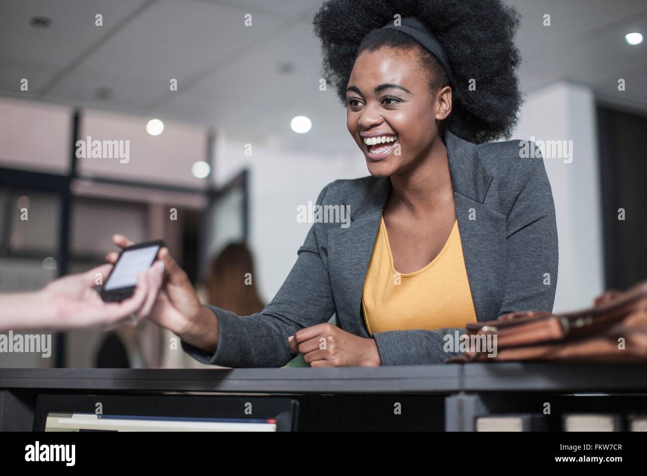 Receptionist handing young businesswomen smartphone at office reception ...