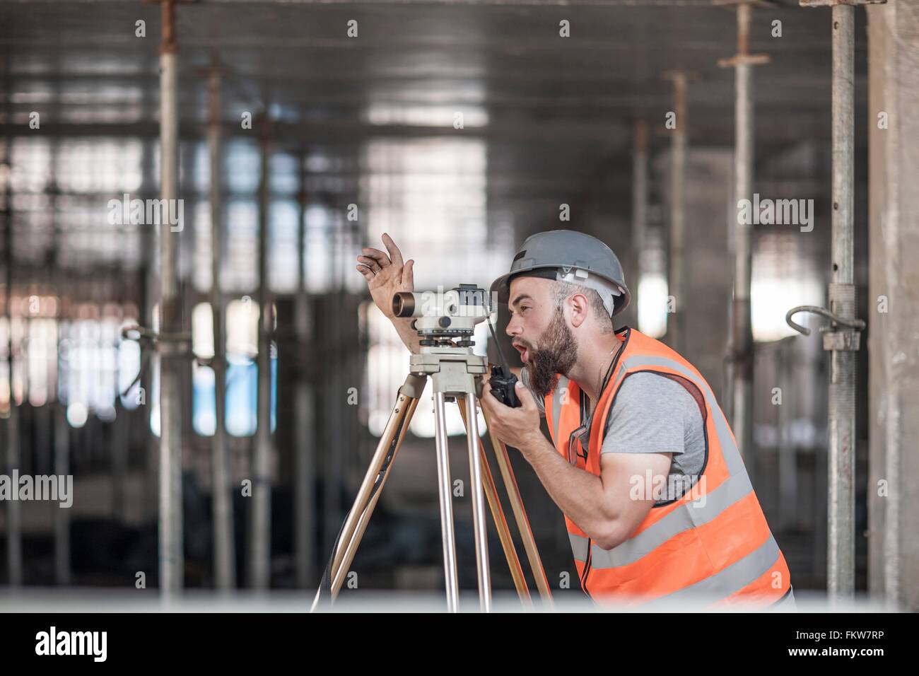 Young male surveyor looking through theodolite giving hand signal on ...