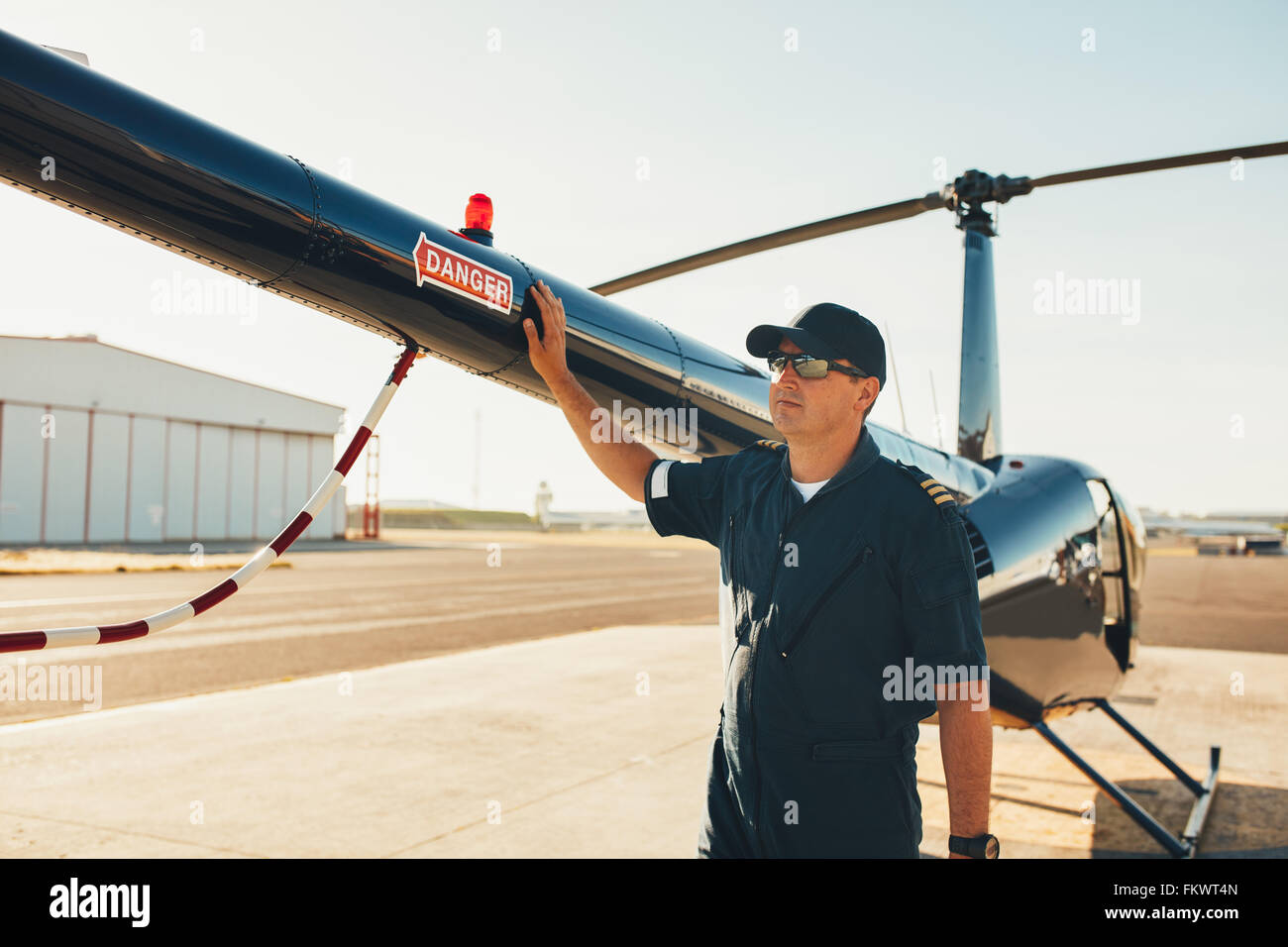 Male pilot standing at the tail of a helicopter and looking away ...