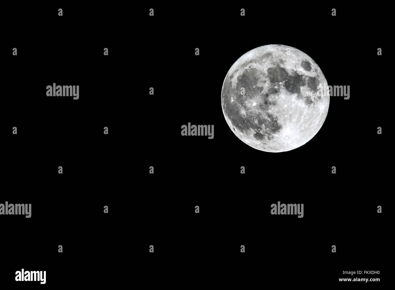 The full Moon is seen isolated on a black background. High contrast ...