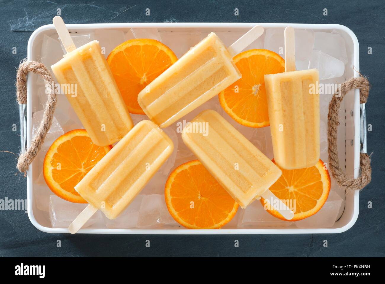 Homemade orange yogurt popsicles in an rustic ice filled tray with ...