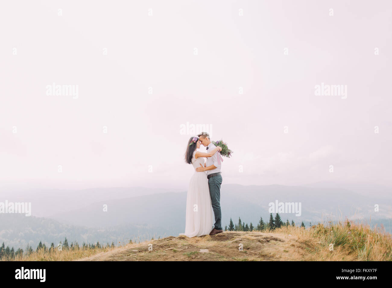Bride and groom softly hug at the mountain peak. Breathtaking photo ...