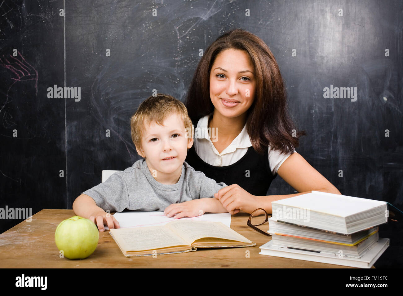 little cute boy with young teacher in classroom studying at blackboard ...