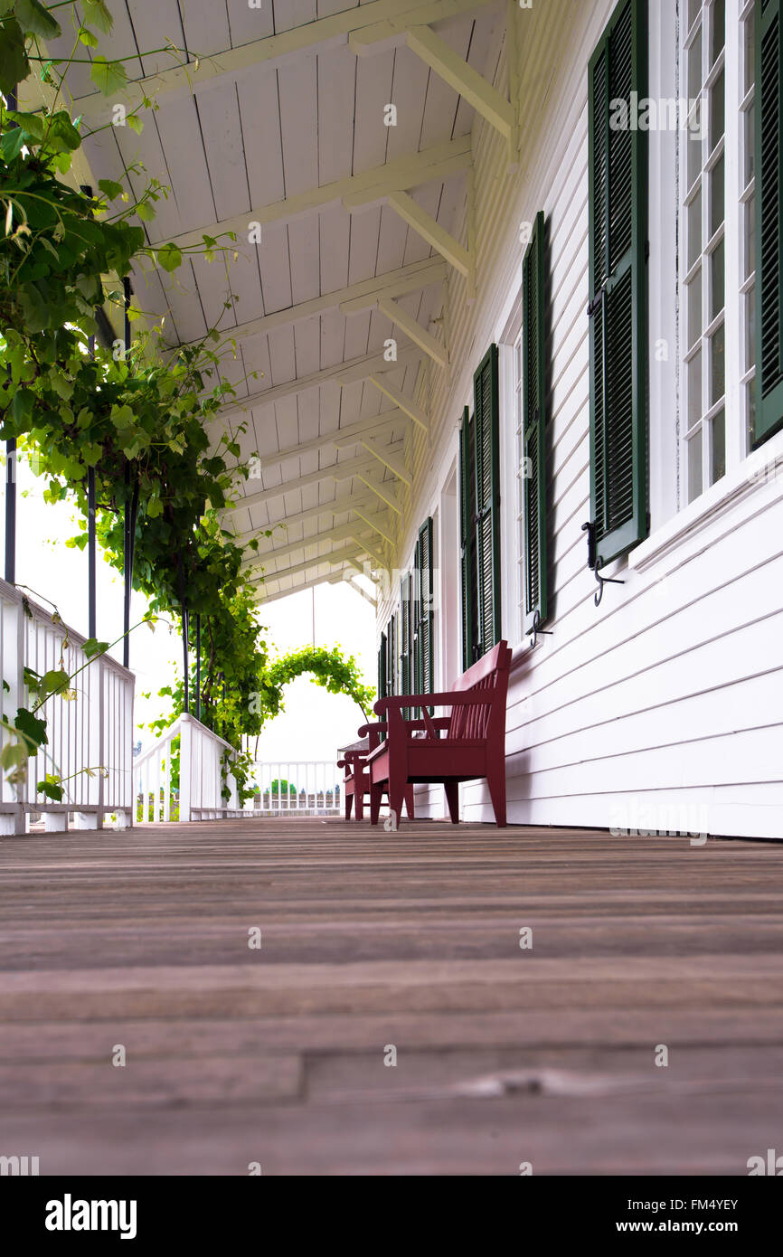 Maroon wooden bench on the covered wooden attic of a large white house ...