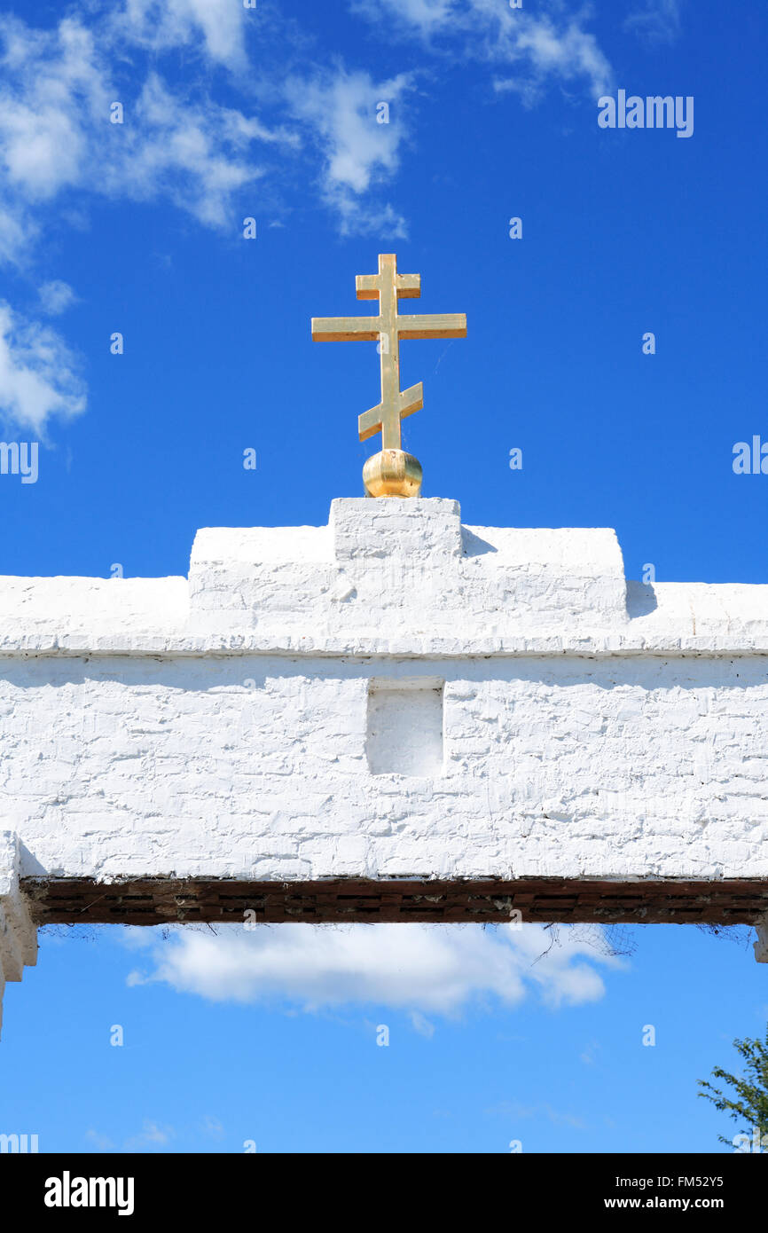 Closeup of golden Orthodox cross on white monastery gates against blue ...