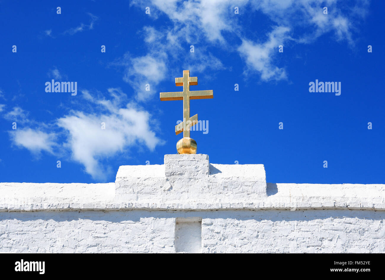 Closeup of golden Orthodox cross on white monastery gate against blue ...