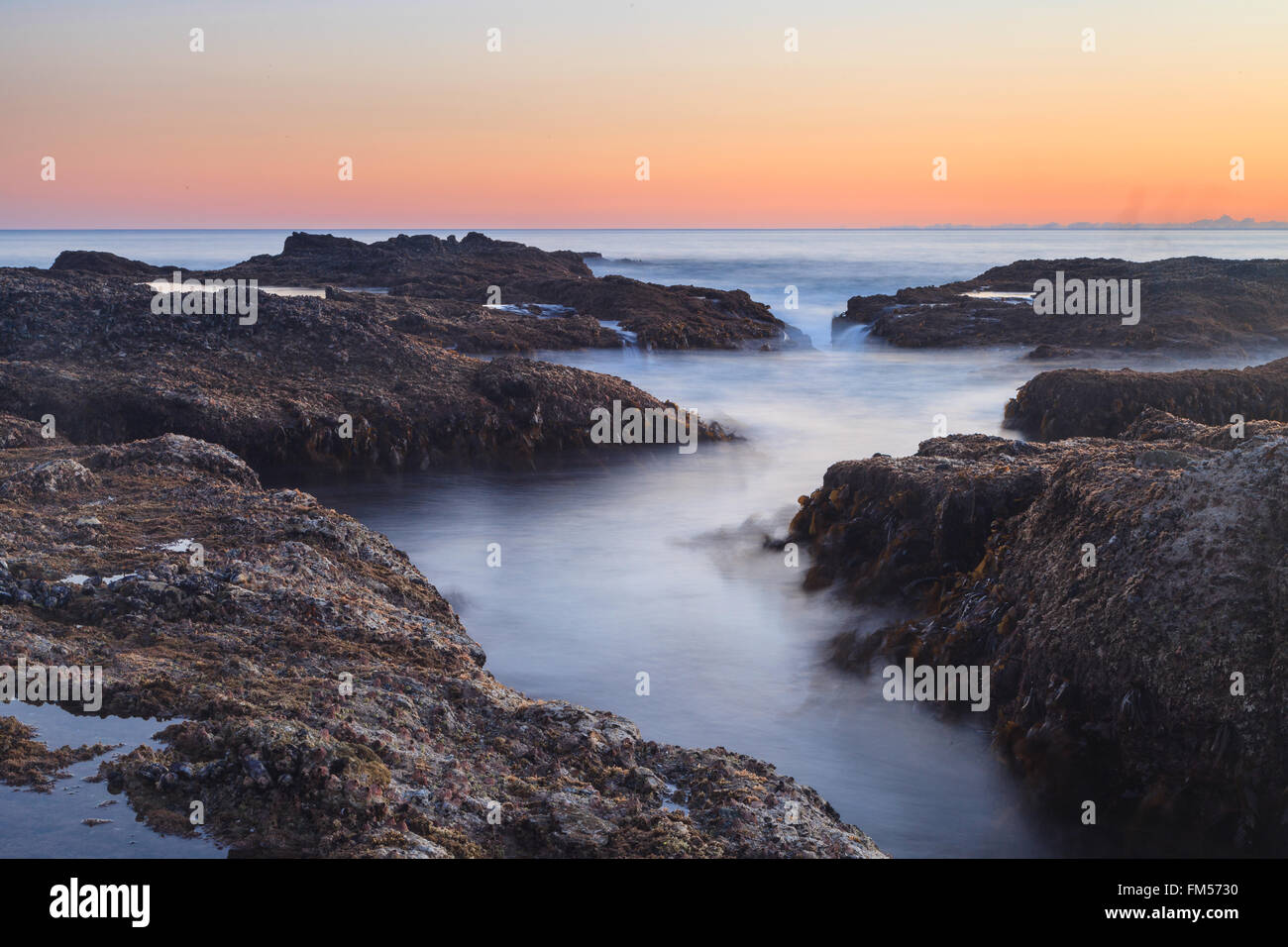 Long exposure of sunset over rocks, giving a mist like effect over ...