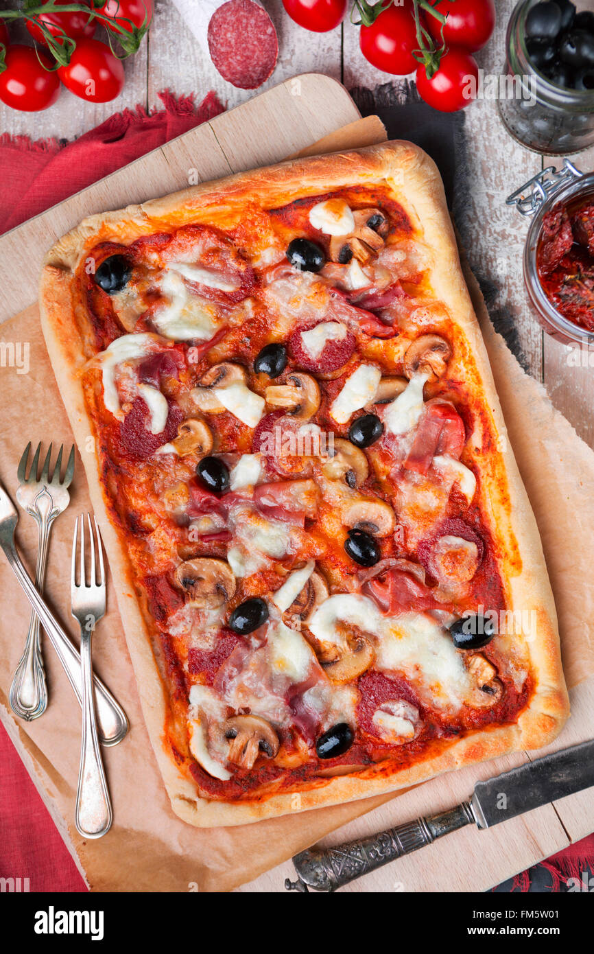 Homemade rectangular pepperoni pizza on a rustic table with ingredients. Photographed from ...