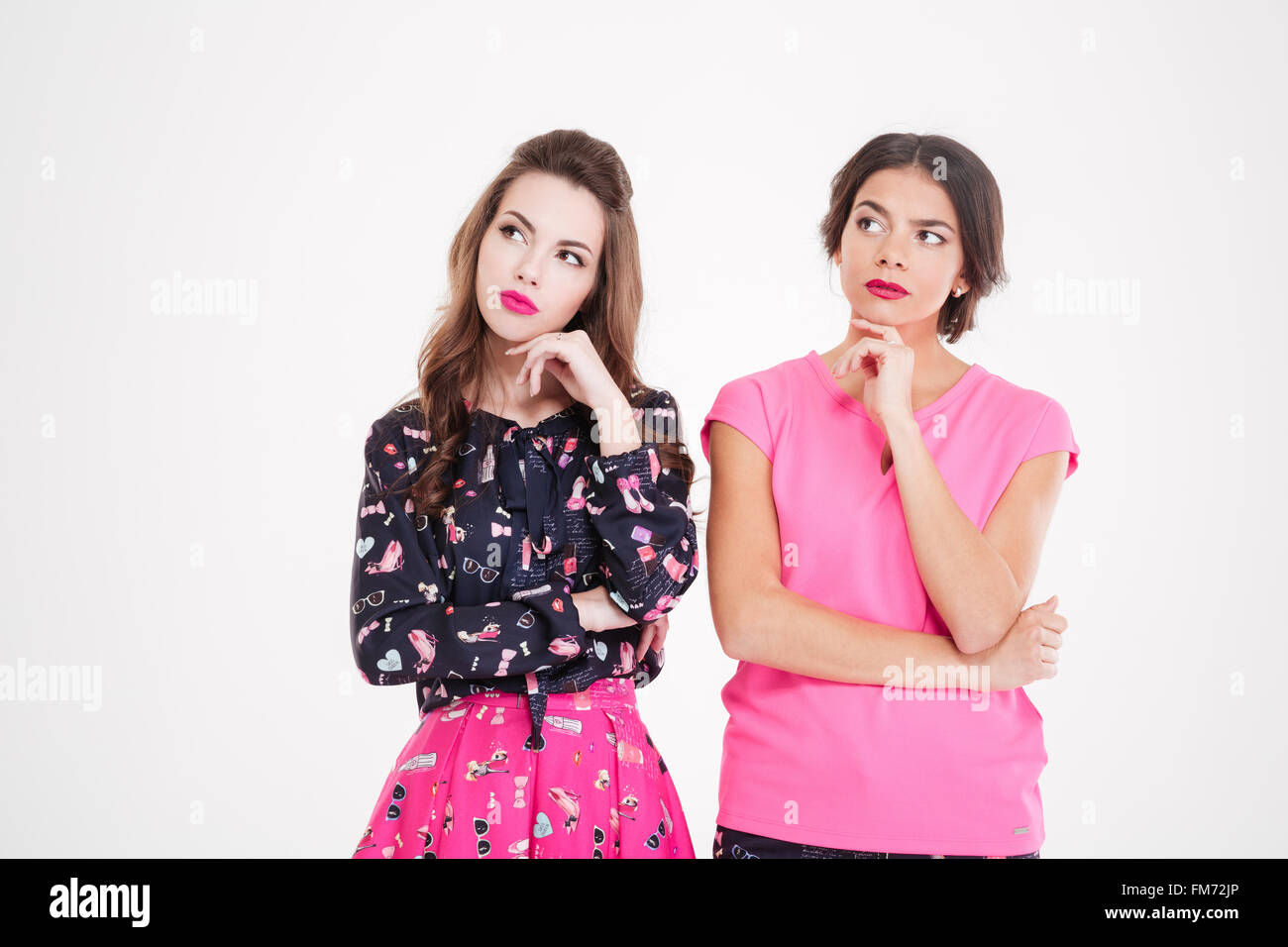 Two pensive beautiful young women standing and thinking over white ...