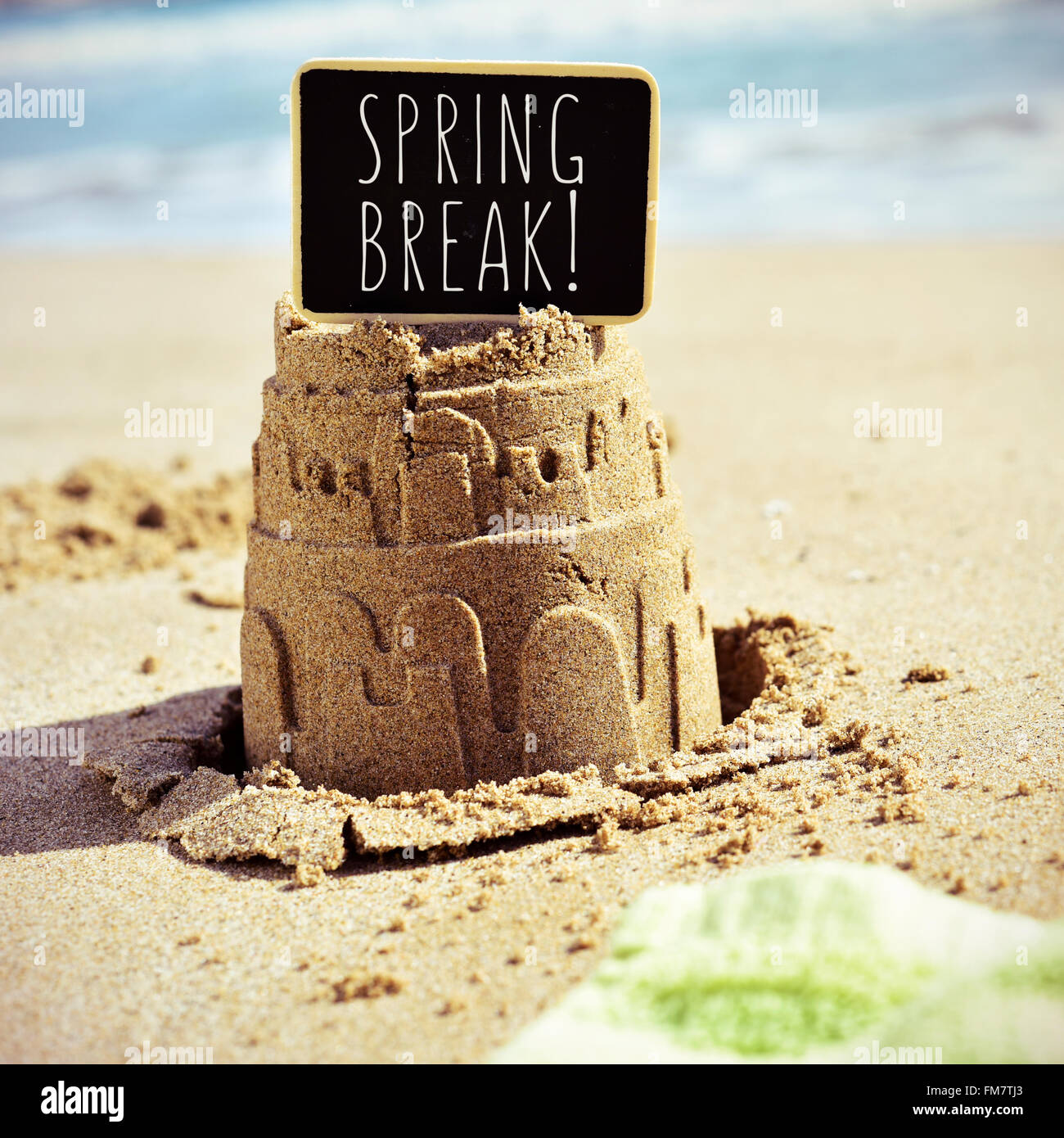 a black signboard with the text spring break placed on a sandcastle, on ...
