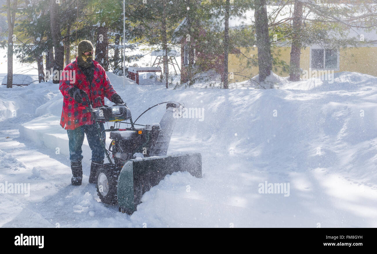 A man dress in winter work wear, operating a snow thrower on a winter ...