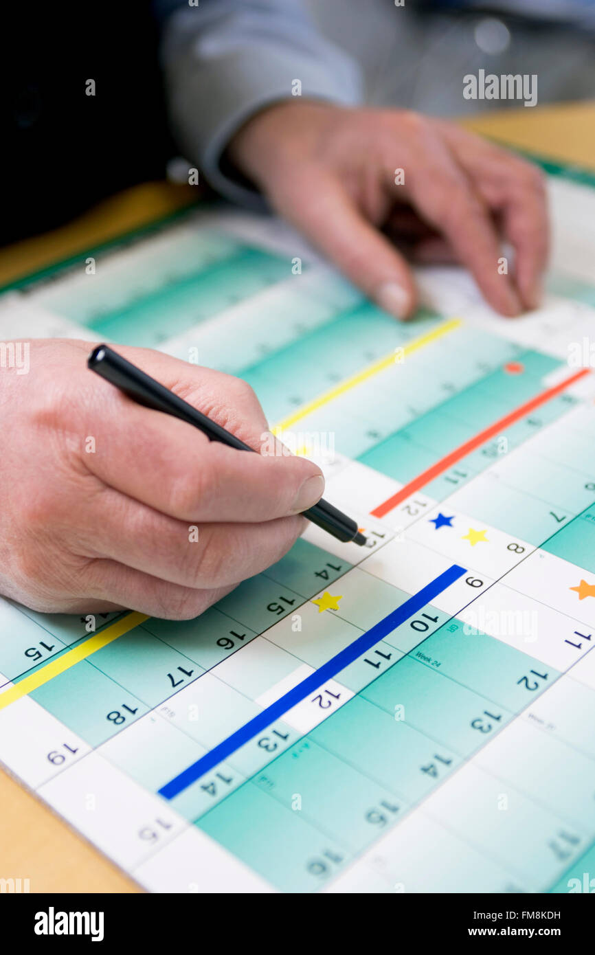 Hands holding pen over calender marked with with star stickers and blue ...