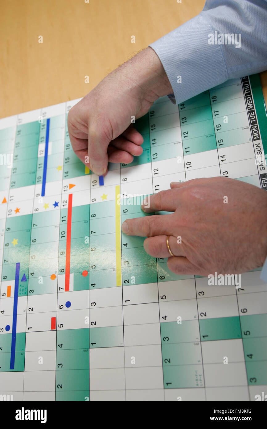 Hands sticking blue sticker on calender marked with stickers in ...