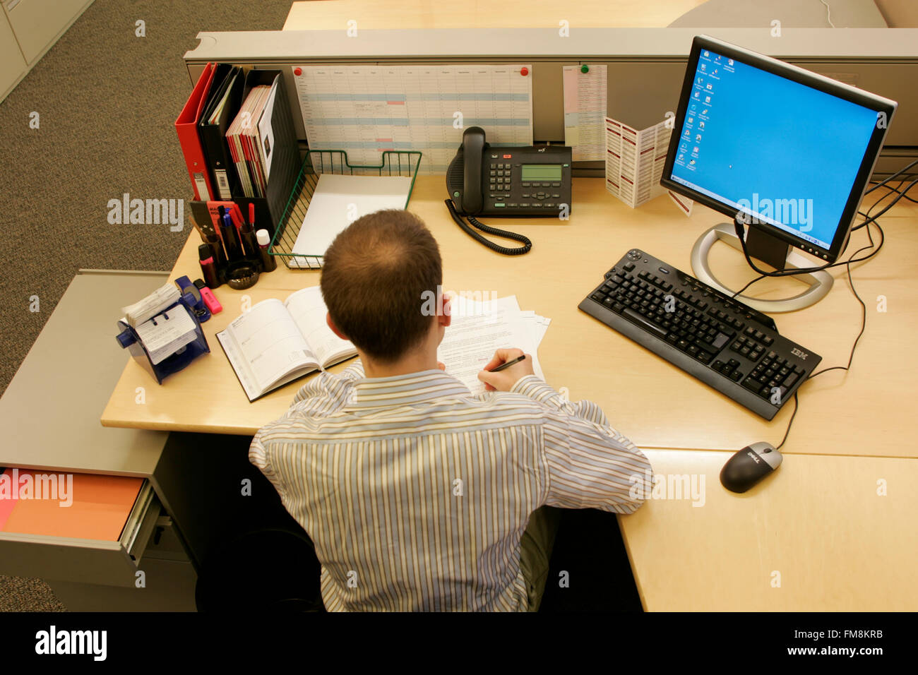 Man writing at desk with computer, telephone and selection of office ...