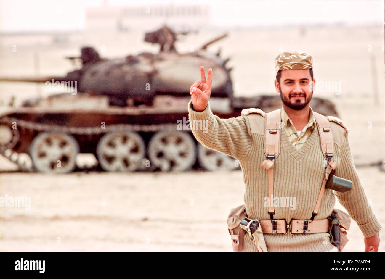 A Qatar soldier walking past a destroyed Iraqi tank flashes the victory ...