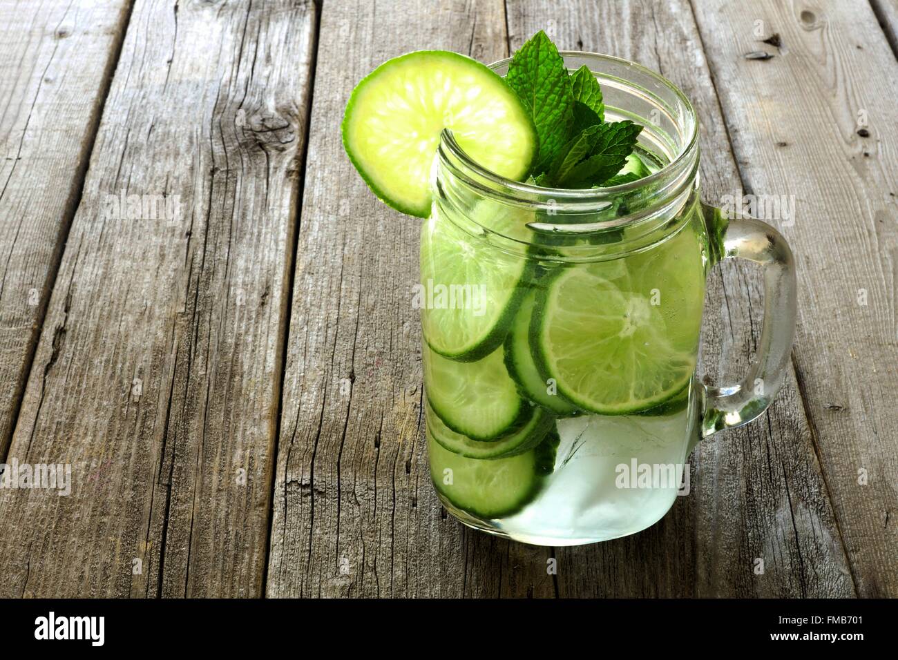 Detox water with lime and cucumbers in a mason jar against a rustic ...